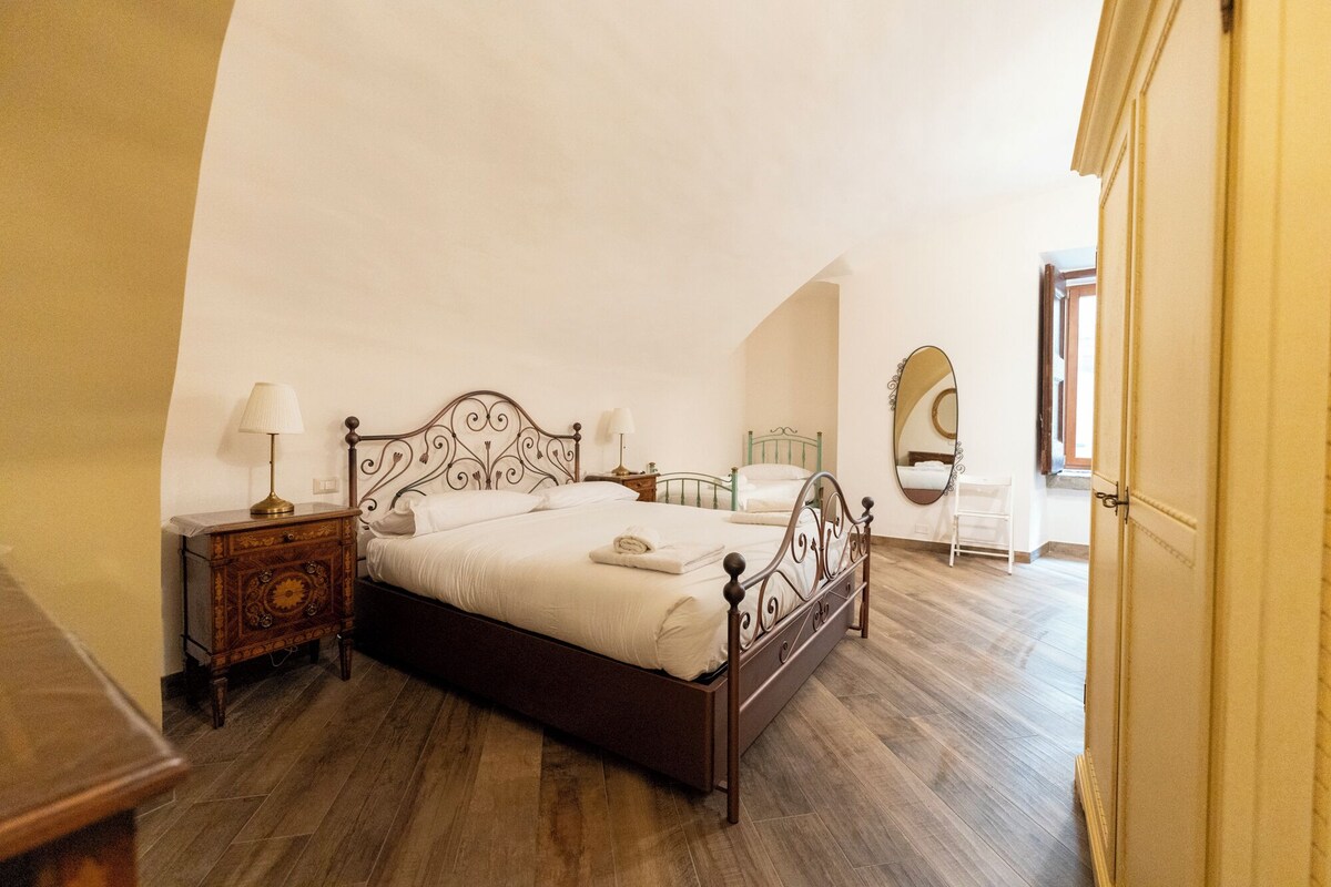 Quarto com cama de madeira, duas mesas de cabeceira com luminárias, um espelho e um guarda-roupa.