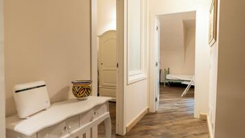 Um corredor com um banco branco, uma tigela colorida e uma porta que dá para outro quarto.