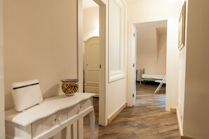 Um corredor com um banco branco, uma tigela colorida e uma porta que dá para outro quarto.