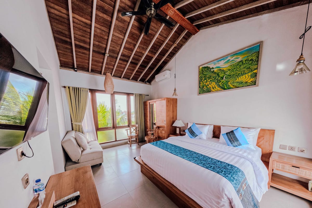 Quarto com uma cama grande, uma escrivaninha, uma cadeira, um ventilador de teto e um quadro na parede.