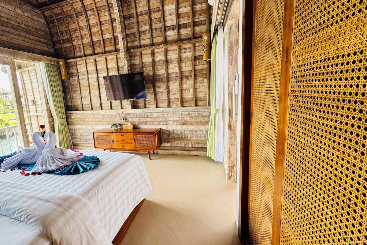 Quarto com cama, cómoda de madeira, televisão na parede e varanda com vista.