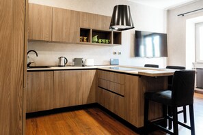 Uma cozinha moderna com armários de madeira, uma luminária pendente preta, um laptop e uma TV de tela plana.