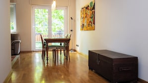 Um quarto com piso de madeira, uma mesa de jantar com cadeiras, um armário de madeira escura e uma janela grande com persianas.