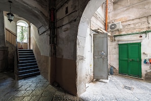 Um corredor arqueado com escada, porta e janela com persiana verde.