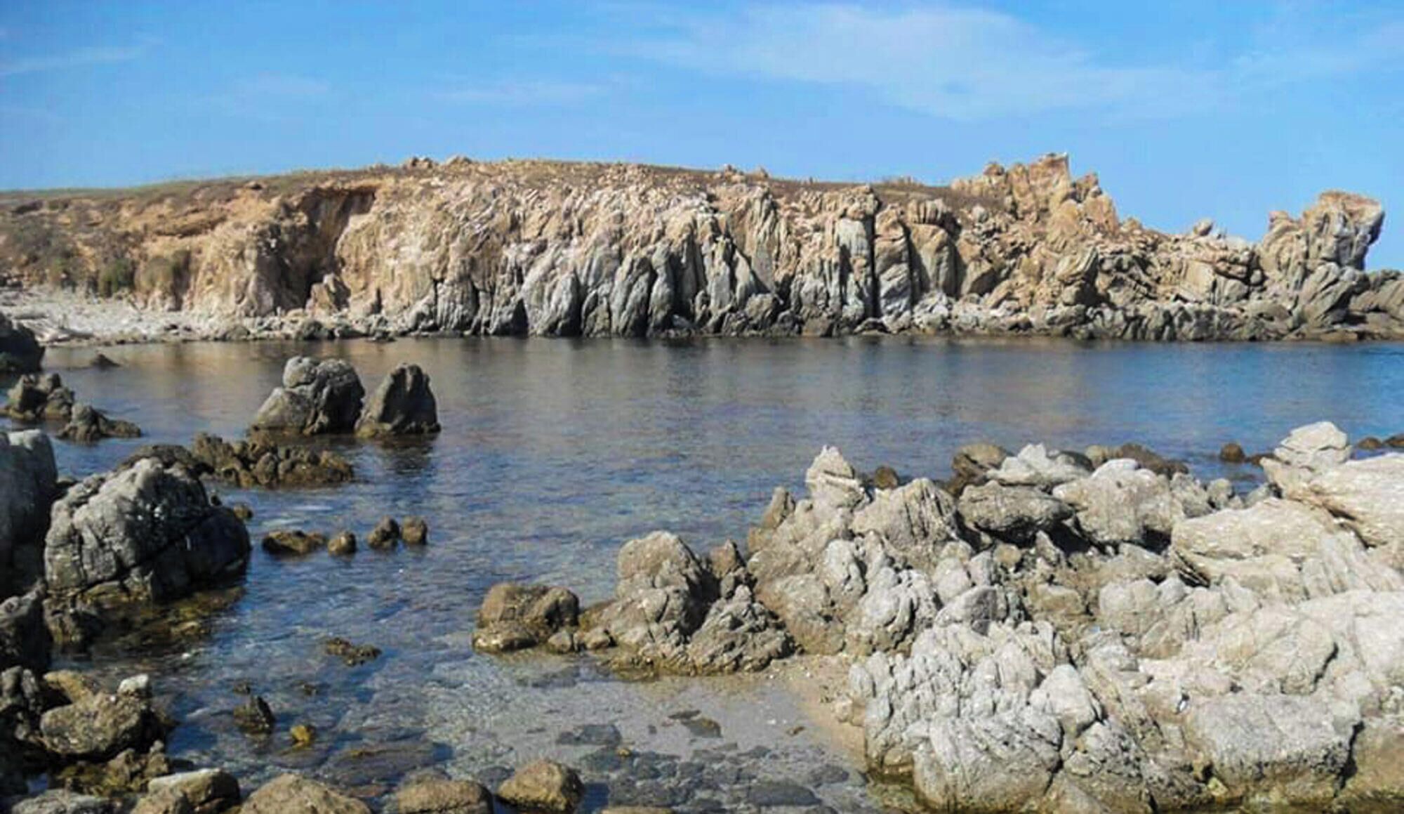 Uma costa rochosa com águas cristalinas e um penhasco ao longe.