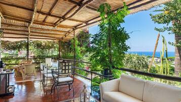 Uma área de estar coberta ao ar livre com vista para o mar, incluindo um sofá, cadeiras e uma mesa.