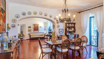 Uma área de refeições com mesa de madeira e cadeiras de vime, um candelabro e uma parede decorada com pratos.