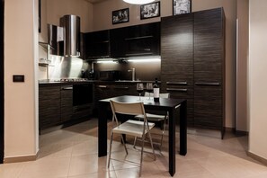 Uma cozinha moderna com armários escuros, coifa de aço inoxidável, micro-ondas e uma área de jantar com mesa e cadeiras.