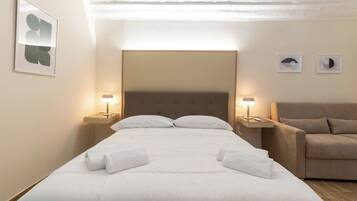 Quarto de hotel com uma cama grande, duas mesas de cabeceira com luminárias, um sofá e obras de arte nas paredes.
