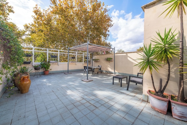Uma área de pátio com pérgola, vasos de plantas e mobiliário de exterior.