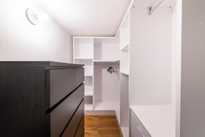 Um closet espaçoso e bem iluminado, com piso de madeira, prateleiras brancas e um armário de madeira escura.