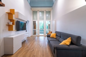 Uma sala de estar moderna com um sofá cinzento, almofadas amarelas, uma TV de tela plana presa a um móvel branco e piso de madeira.