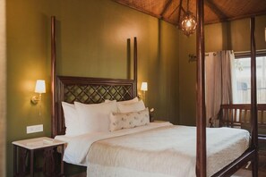 Uma cama de dossel com cabeceira de madeira, duas luminárias de cabeceira e uma janela com cortinas.