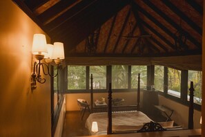 Quarto com uma cama, uma mesa e uma cadeira, com vista para o verde lá fora.