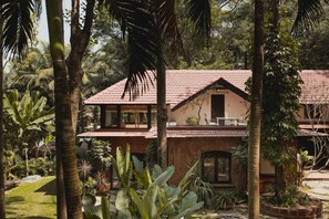 Um edifício de dois andares com telhado de cerâmica, rodeado por vegetação exuberante e palmeiras.
