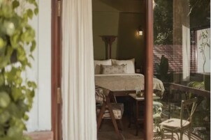 Quarto com cama, mesa de cabeceira e abajur. Varanda com cadeiras e vista para o exterior.