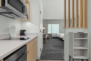Quarto de hotel moderno com cozinha compacta, cama, escrivaninha e vista para o exterior.