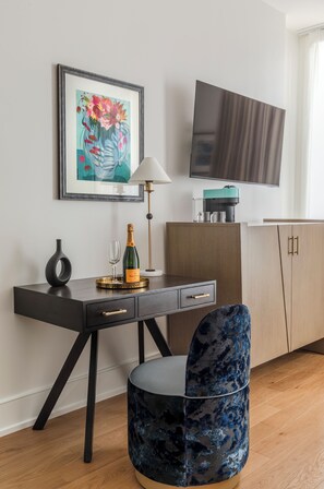Quarto moderno com escrivaninha, cadeira, televisão, obra de arte emoldurada e máquina de café.