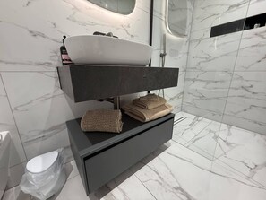 Casa de banho moderna com revestimento em mármore, lavatório branco, toucador escuro e sanita.