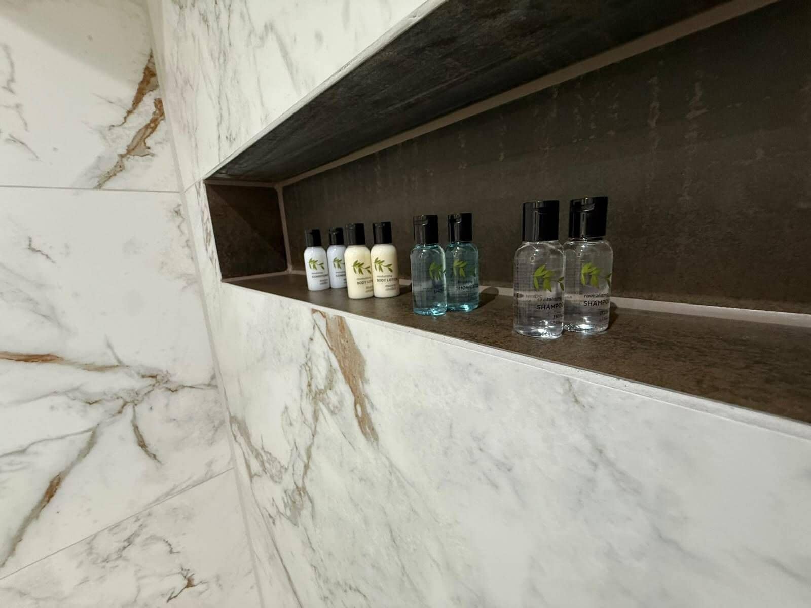 Pared de mármore com uma prateleira contendo várias garrafas de shampoo e loção corporal.