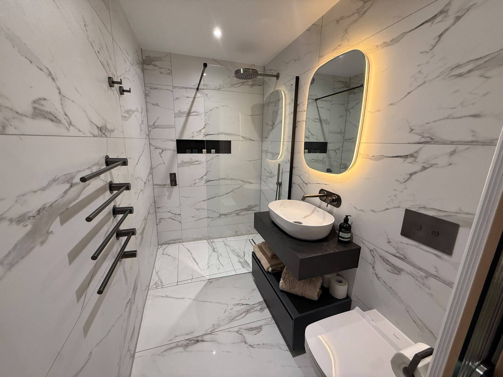 Uma casa de banho moderna com lavatório de mármore branco, toucador preto e cabine de duche em vidro.