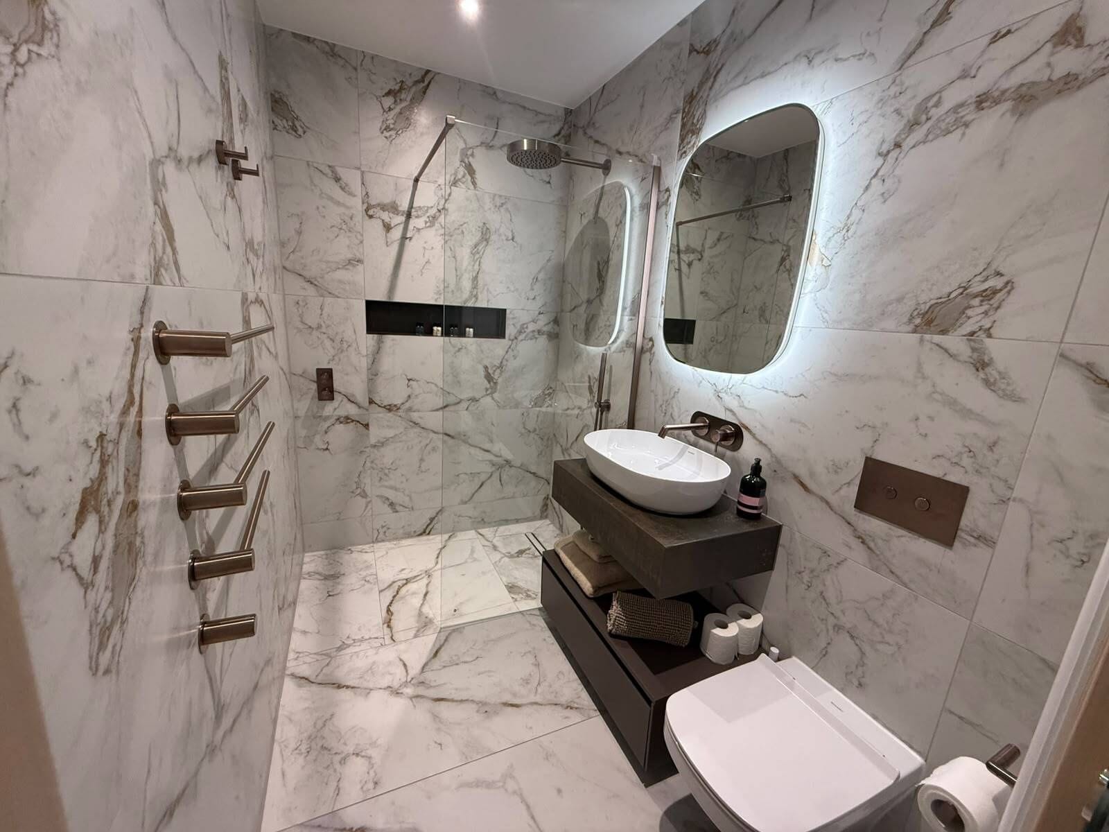 Um banheiro moderno com piso de mármore, pia independente, chuveiro e vaso sanitário.