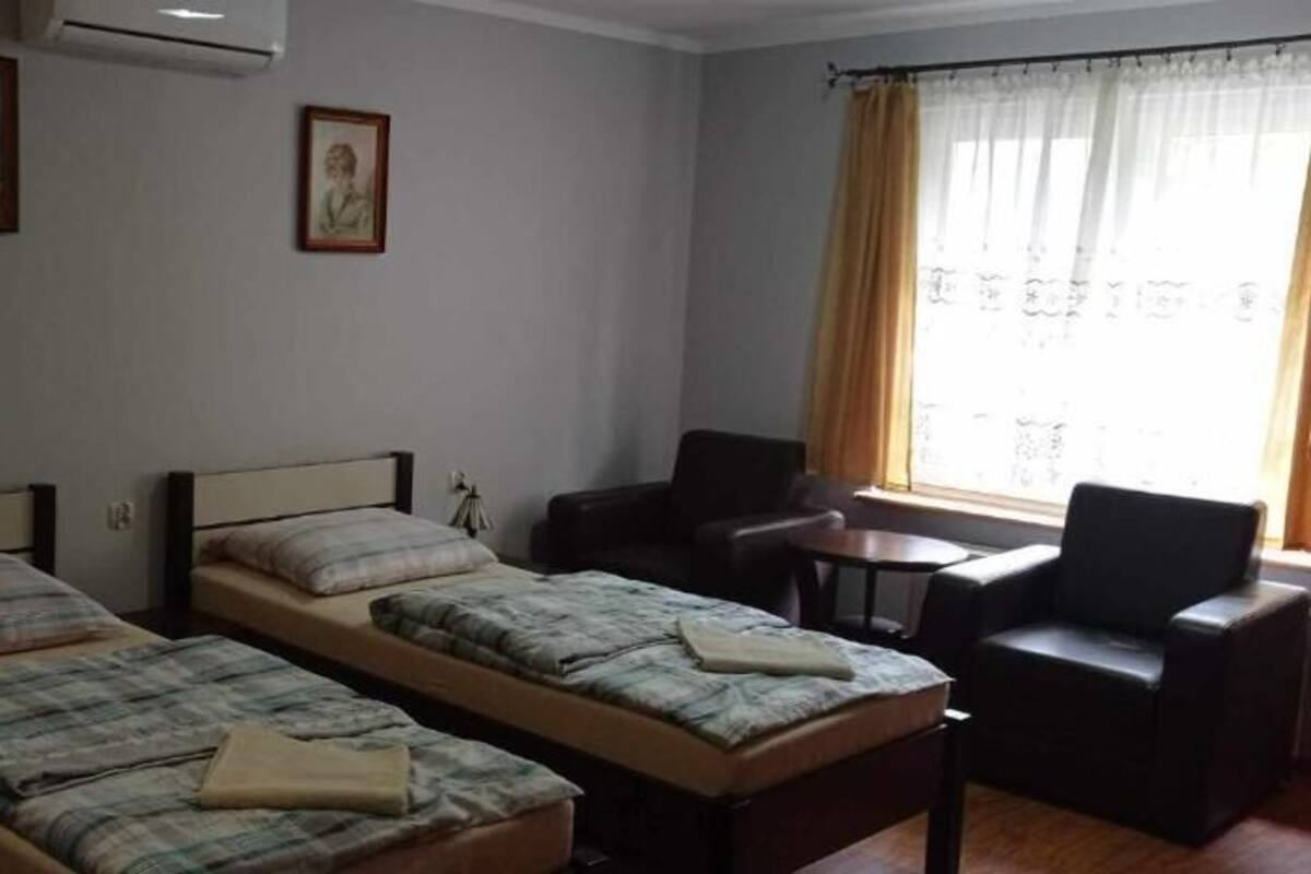 Quarto com duas camas de solteiro, uma mesinha, uma cadeira e uma janela com cortinas.