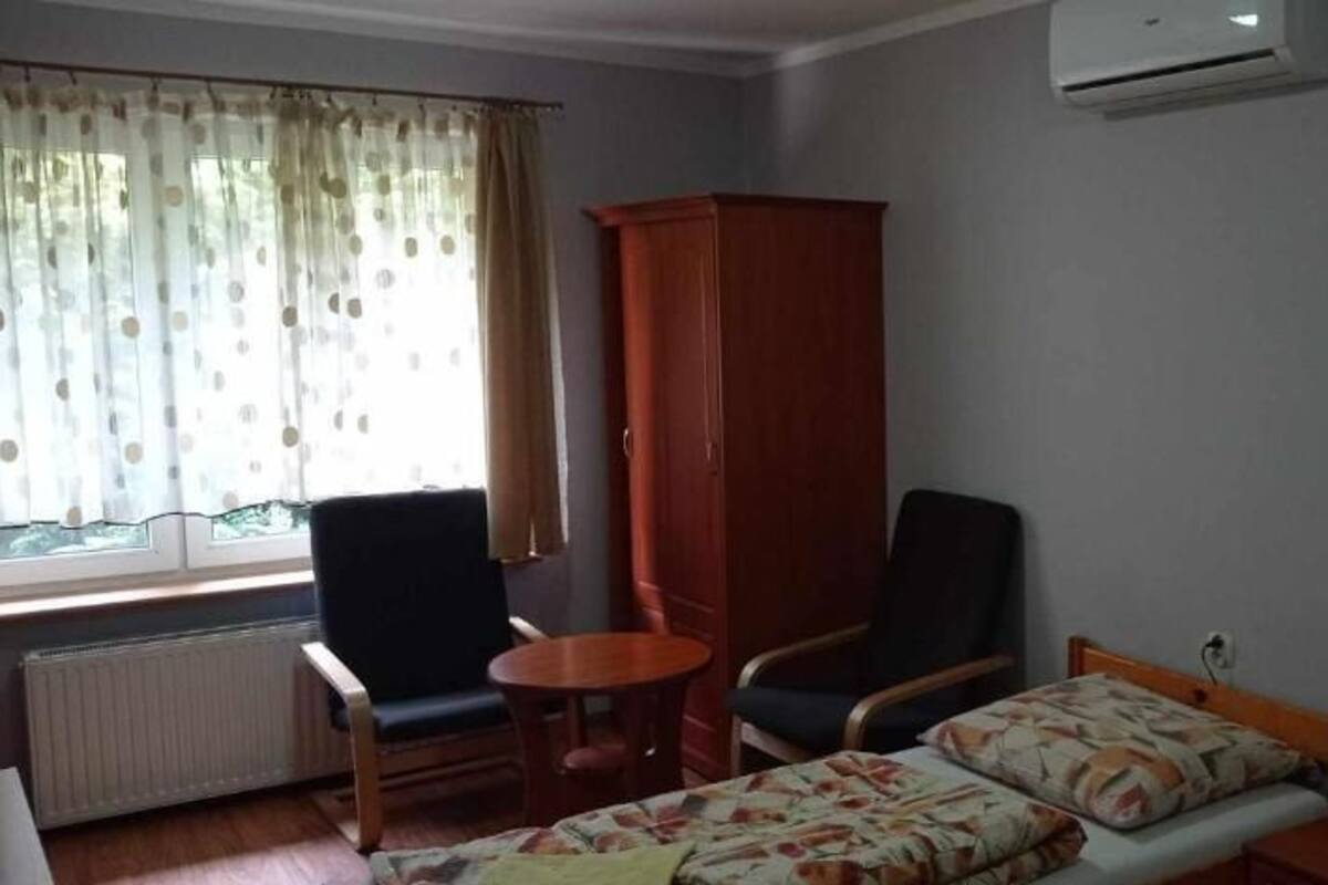 Quarto com uma cama, duas cadeiras, uma mesinha, radiador e ar condicionado.