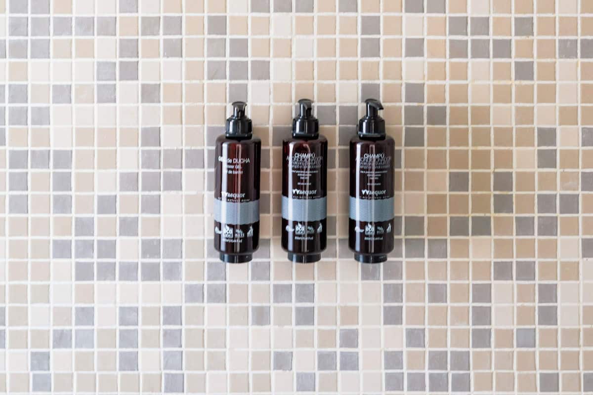 Três garrafas de shampoo sobre um revestimento de azulejos.