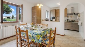 Uma sala de jantar com uma mesa posta para quatro pessoas, uma janela com vista e uma cozinha ao fundo.