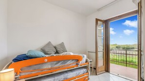 Quarto com cama, almofadas, abajur e vista através de uma porta aberta.