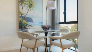 Uma sala de jantar com uma mesa redonda, quatro cadeiras, uma tigela e uma pintura representando uma praia.