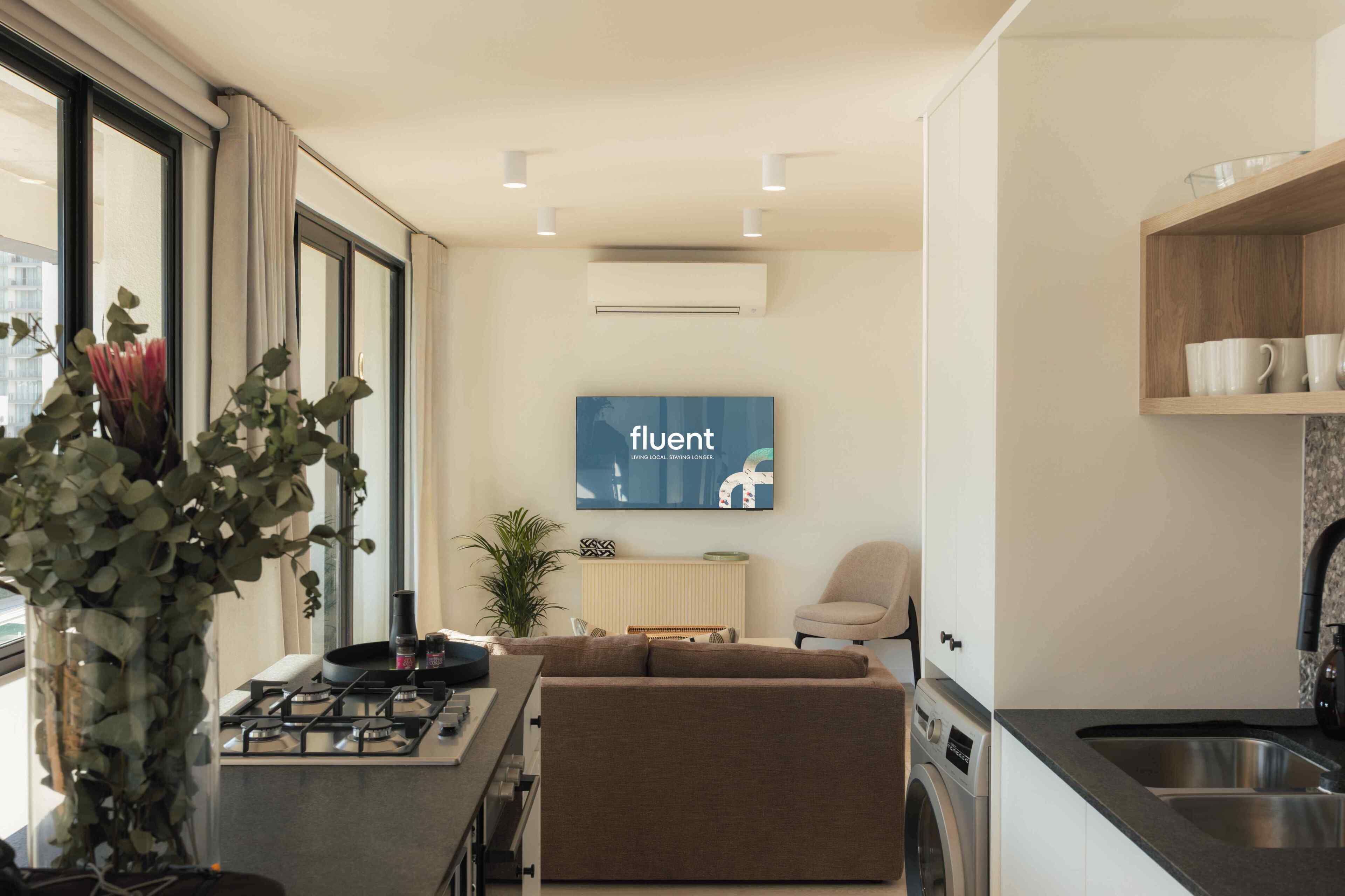Uma sala de estar moderna com sofá, televisão de tela plana na parede, cozinha com fogão e pia.