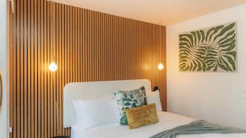 Uma cama com cabeceira, duas almofadas, um cobertor e uma luminária fixada na parede.