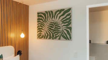 Um quarto com parede de ripas de madeira, parede branca com arte de folha verde, uma cadeira branca e um aparelho de iluminação.