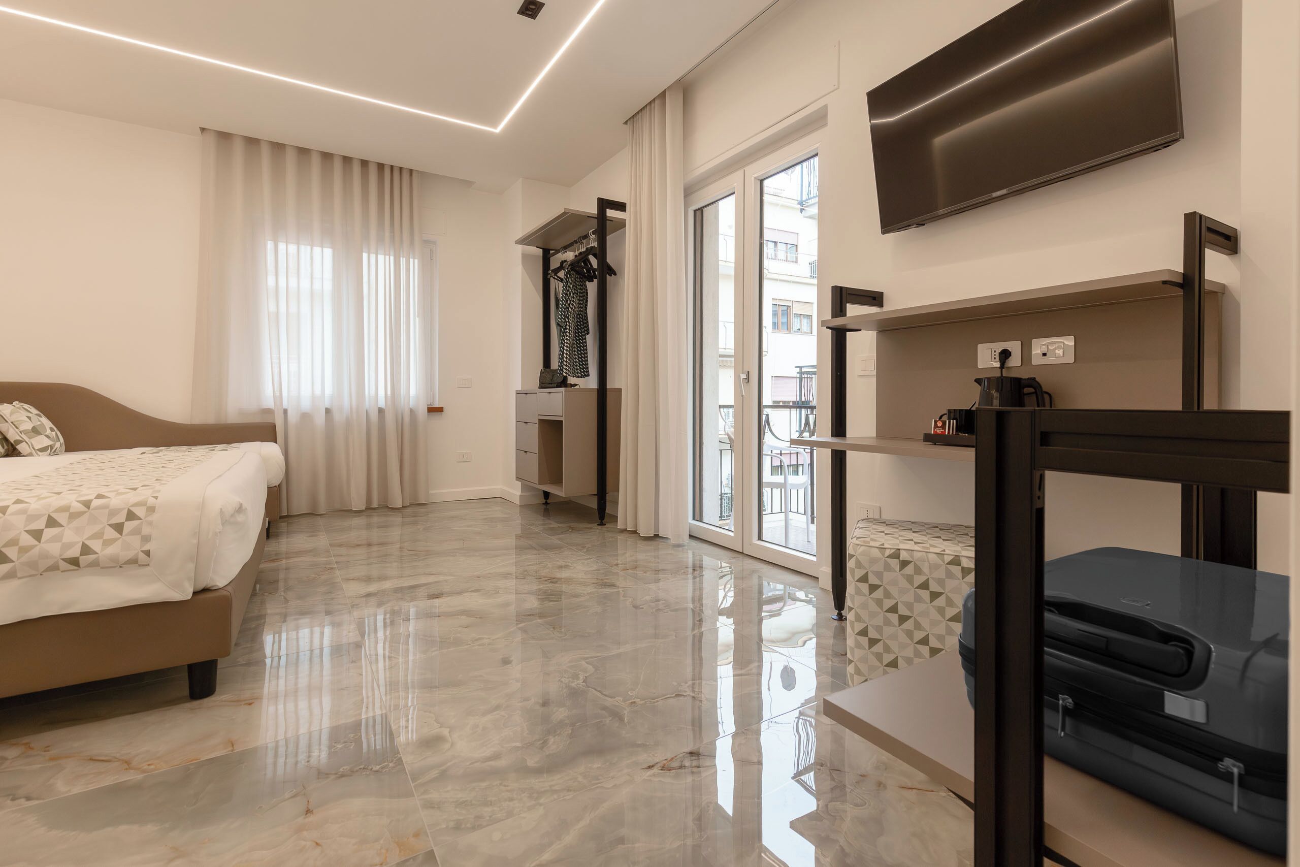 Quarto de hotel moderno com cama, televisão de tela plana, escrivaninha com impressora, guarda-roupa e varanda com vista.