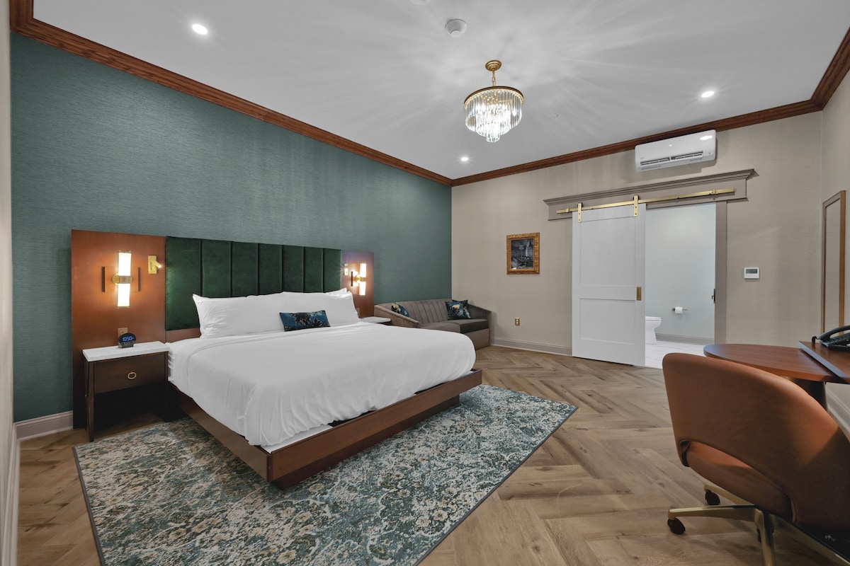 Quarto de hotel com cama, escrivaninha, cadeira, guarda-roupa e banheiro.