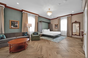 Quarto de hotel com cama, sofá, poltrona e mesa de centro de madeira.