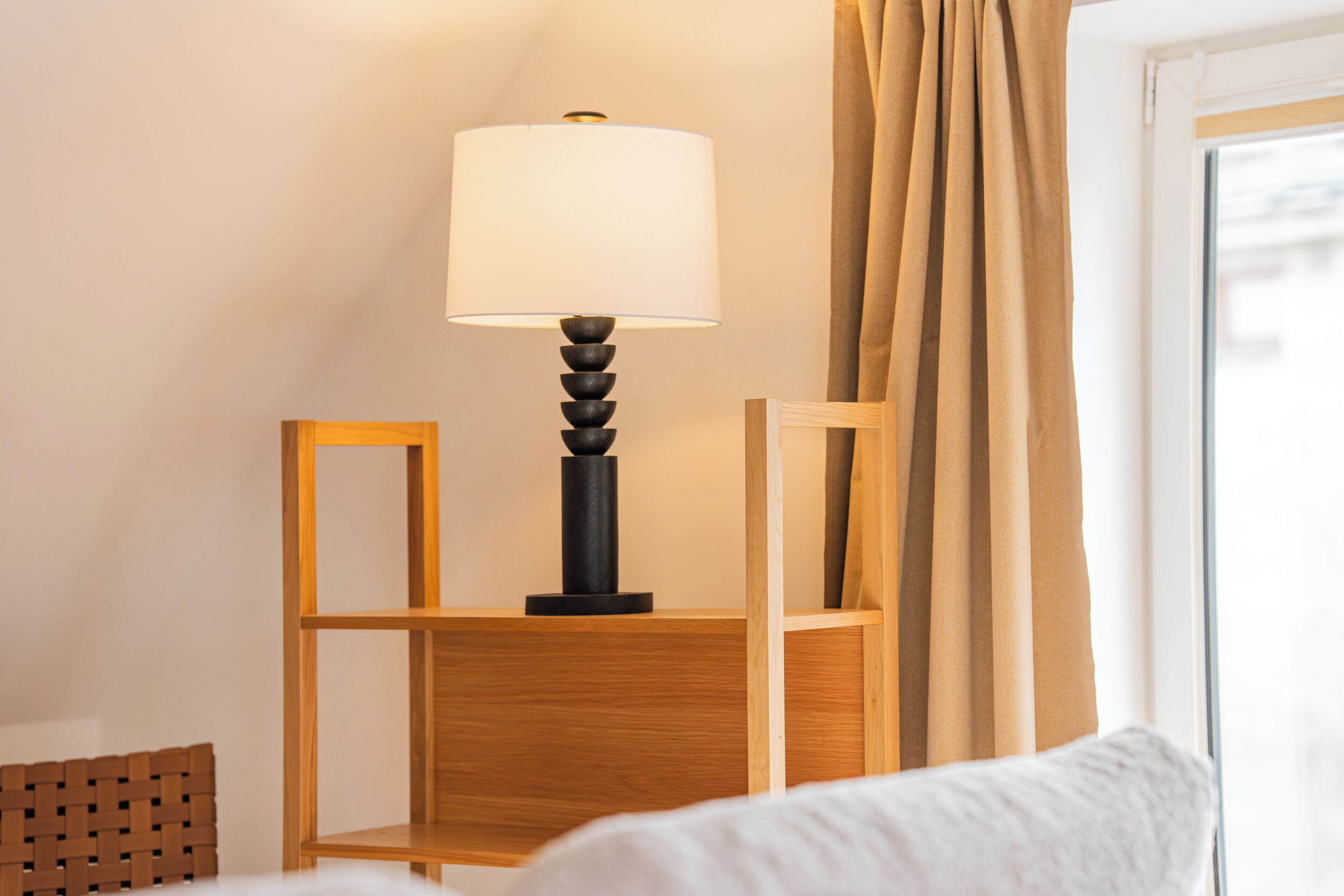 Quarto com uma luminária em um suporte de madeira, um sofá branco e uma janela com cortinas.