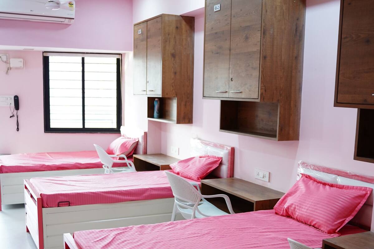 Quarto com duas camas, ventilador de teto, armários de madeira e uma janela.