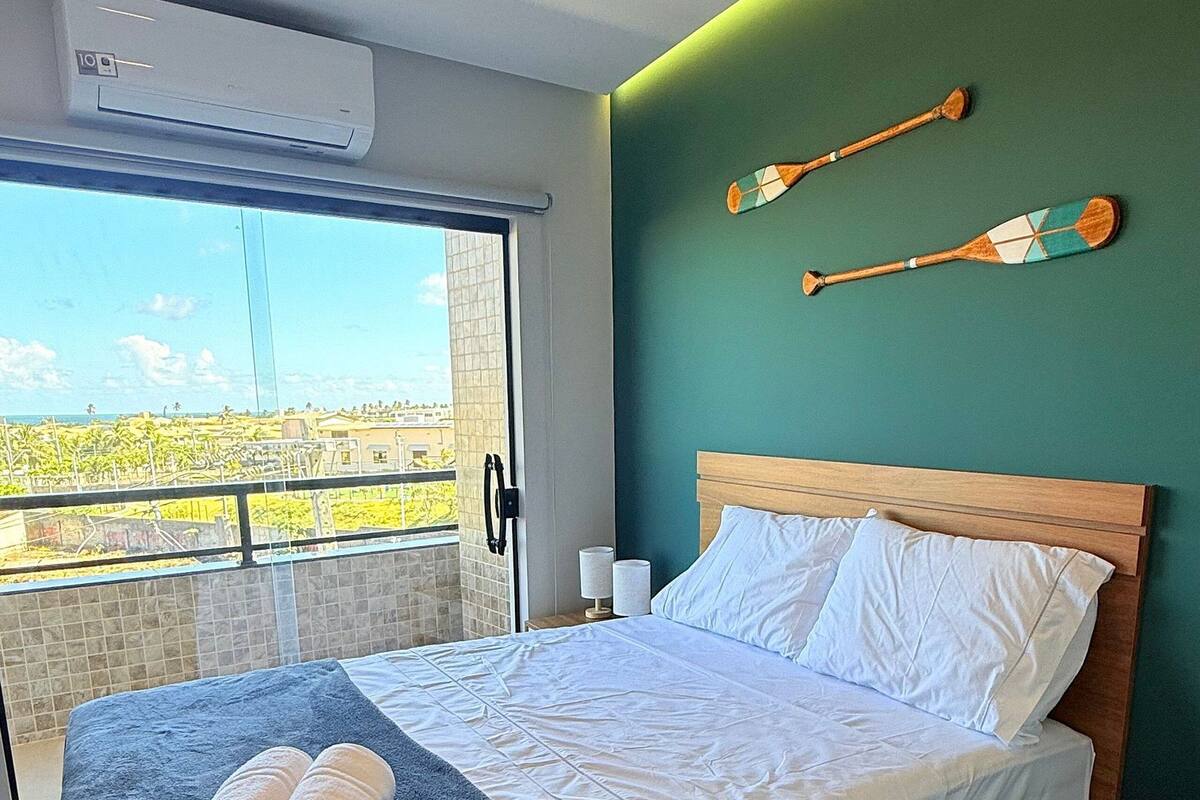 Quarto de hotel com uma cama, vista através de uma grande janela e uma parede verde.