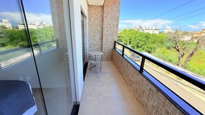 Uma varanda com mesa e cadeiras, vista para a rua e prédios ao fundo.