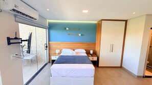 Quarto de hotel com cama, cabeceira de madeira, guarda-roupa, TV fixada na parede e ar condicionado.