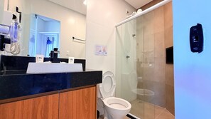 Uma casa de banho moderna com cabine de duche em vidro, sanita branca e bancada preta com espelho.