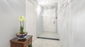 Um corredor com uma porta branca, um candeeiro fixado na parede e um quadro emoldurado.