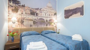 Quarto de hotel com cama, mesa de cabeceira, vaso com flores e um mural na parede retratando uma paisagem urbana.