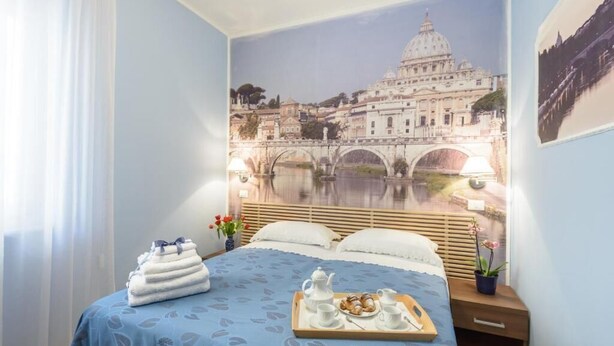 Quarto de hotel com cama, bandeja de itens de café da manhã e um mural de um edifício histórico.