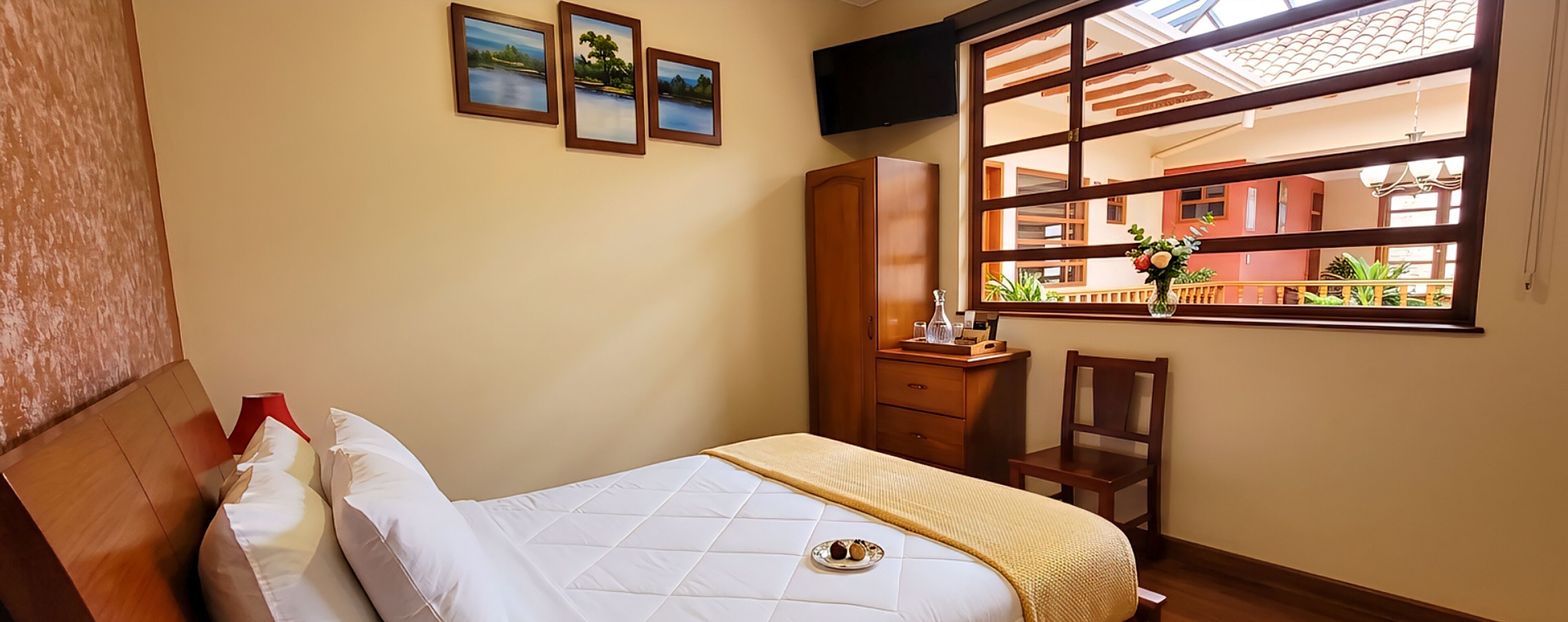 Quarto com cama, escrivaninha, cadeira, guarda-roupa e janela com vista para o exterior.