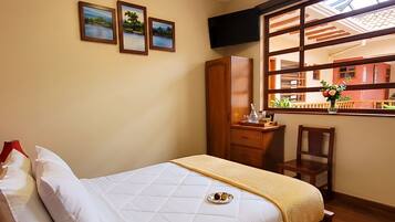 Quarto com cama, escrivaninha, cadeira, guarda-roupa e janela com vista para o exterior.
