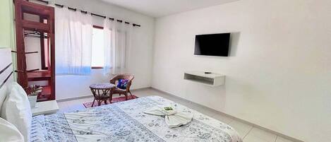 Quarto com cama, televisão, cadeira e janela com cortinas.